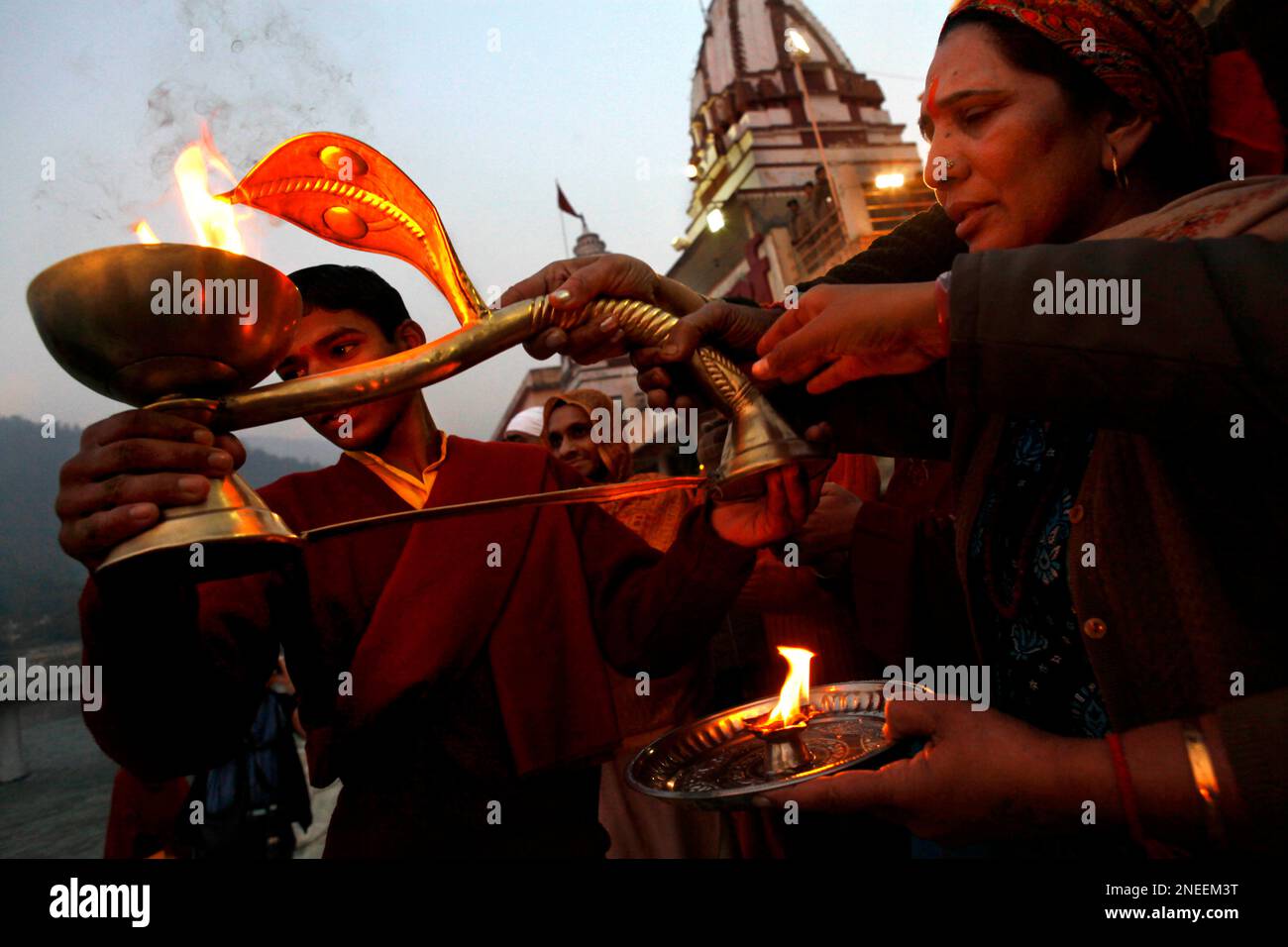 Hindu worshippers reach out to touch a ceremonial oil lamp during the ...