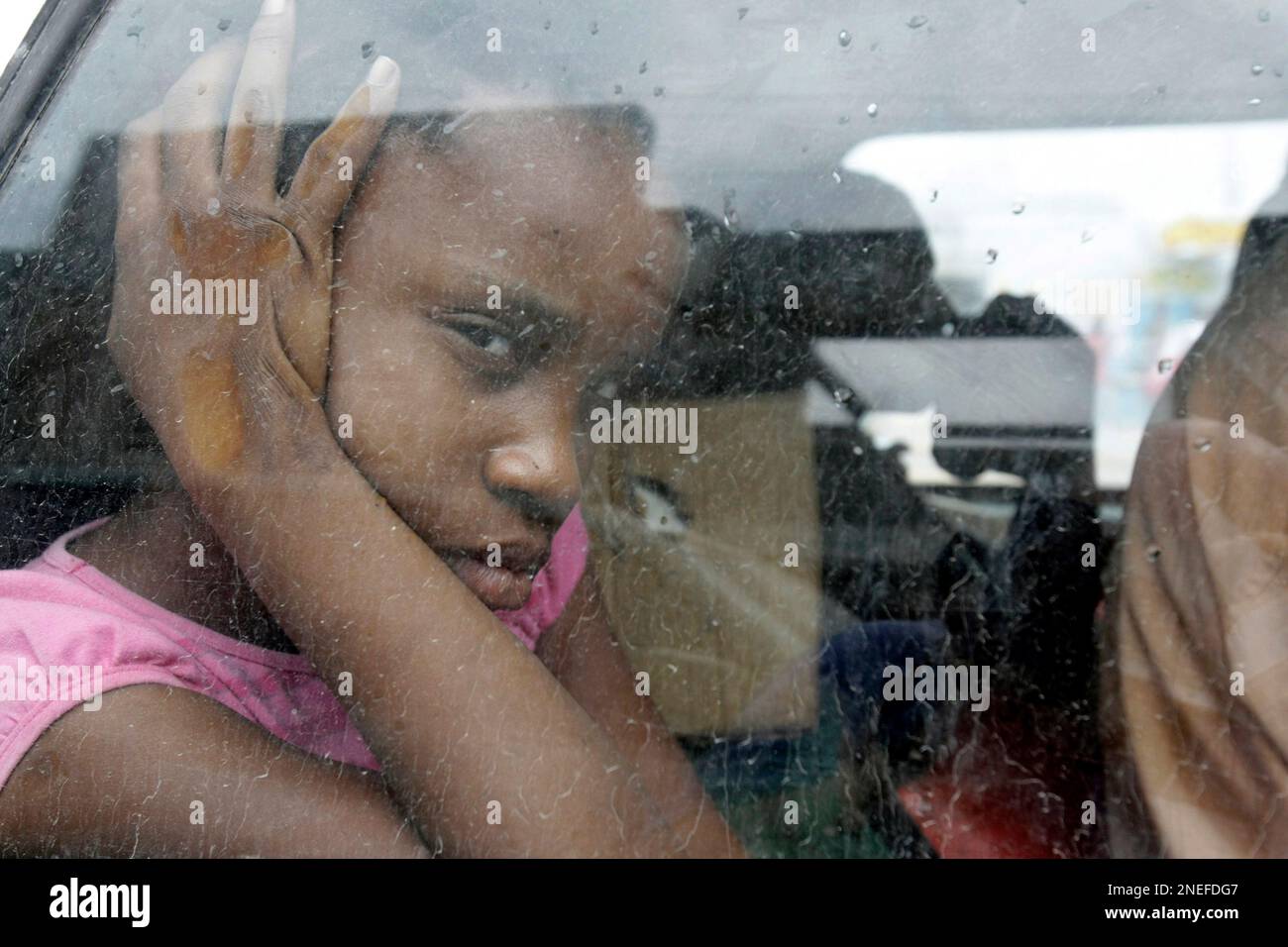 A young earthquake survivor covers her ears as she peers from a bus ...