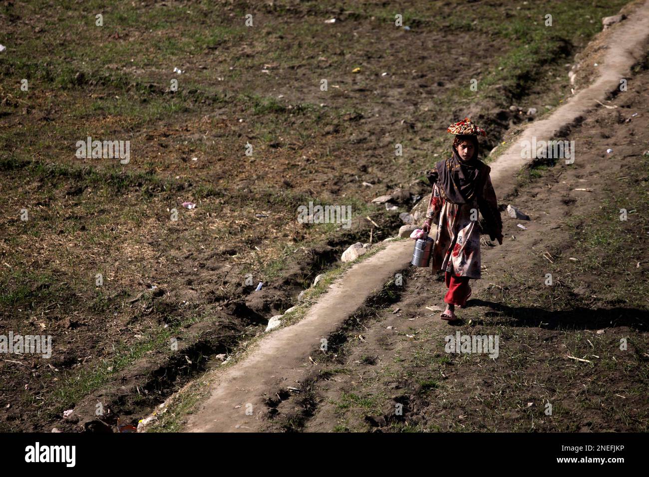An Afghan girl walks along a path with a pot of tea and carrying food ...