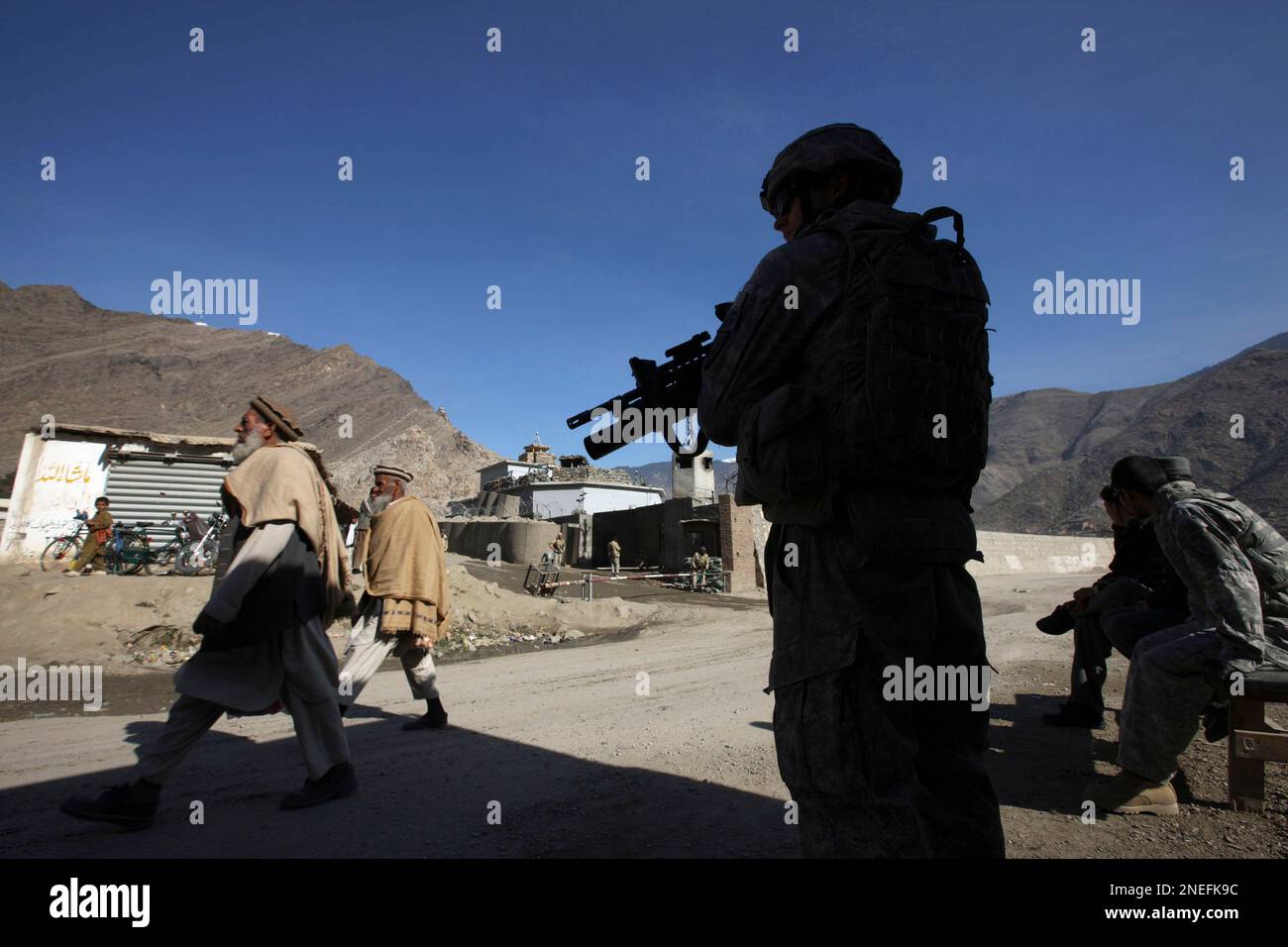Afghan men walk past U.S. Army soldiers manning a checkpoint on the ...