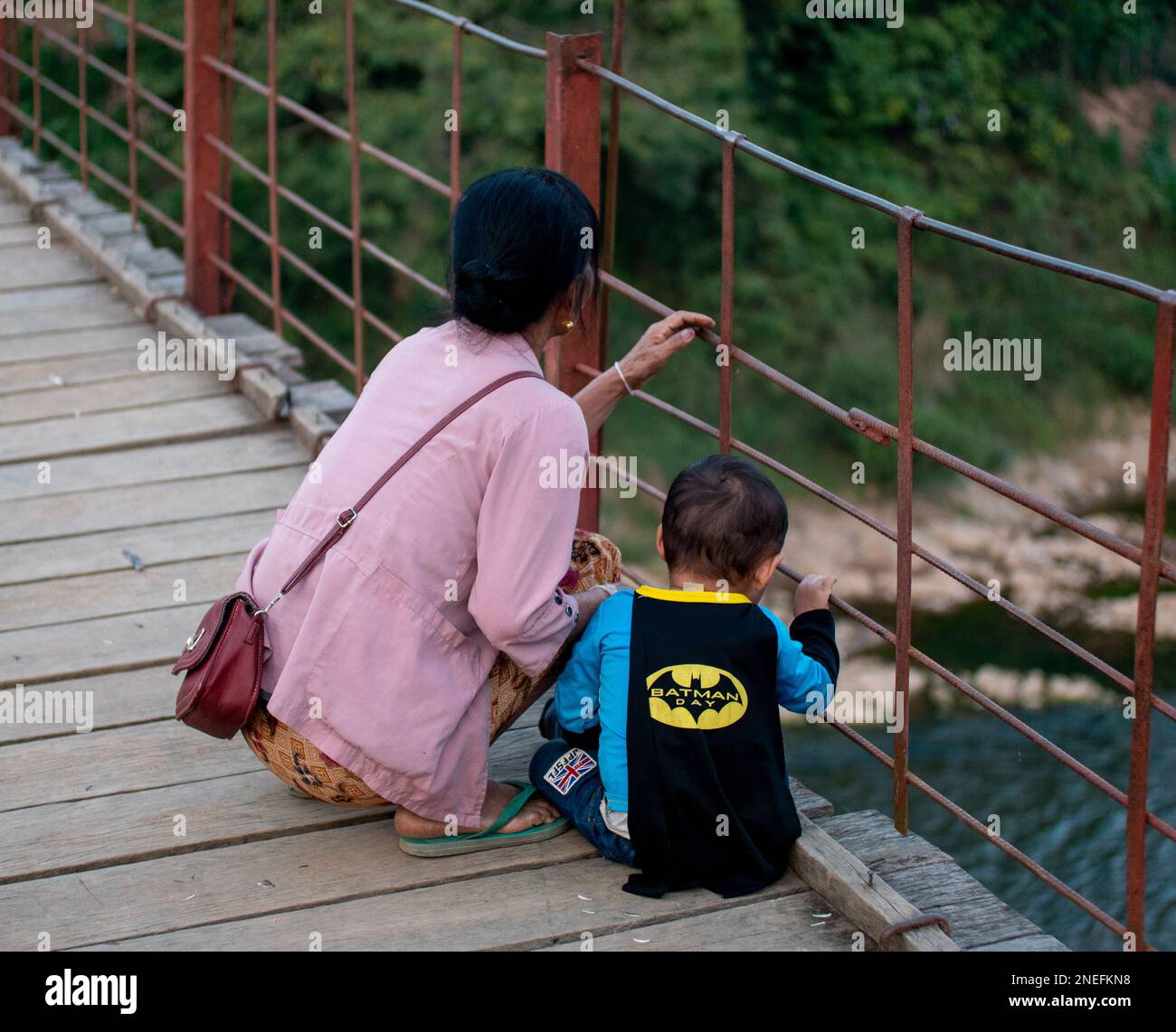 A boy dressed as batman and his grandmother look out over a river from ...