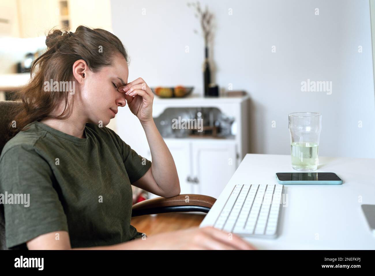 Tired woman sitting at desk at home touching nose bridge with her hand ...