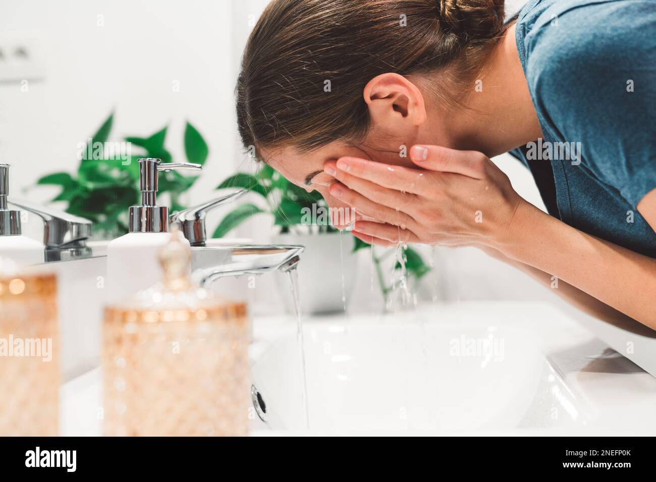 Close up side view woman leaning down in the sink washing her face with ...