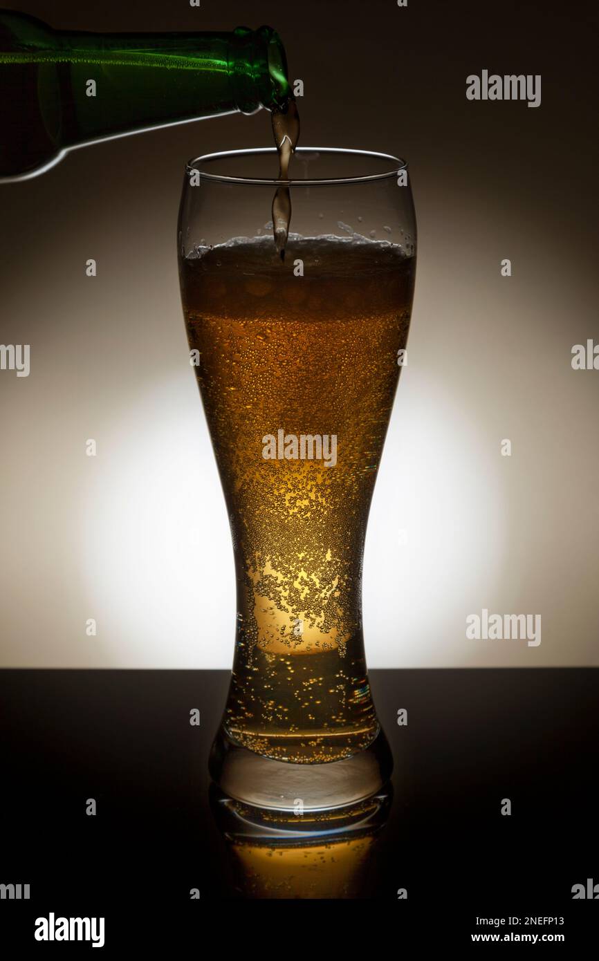 Bottle of lager beer being poured into a backlit glass Stock Photo - Alamy