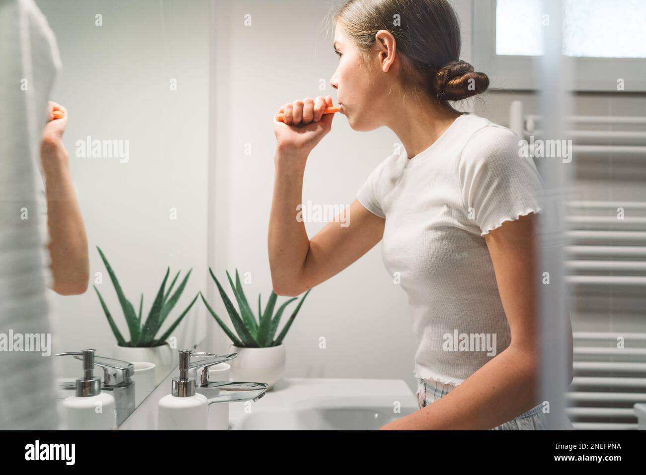 Side view of woman standing in front of a mirror in the bathroom ...