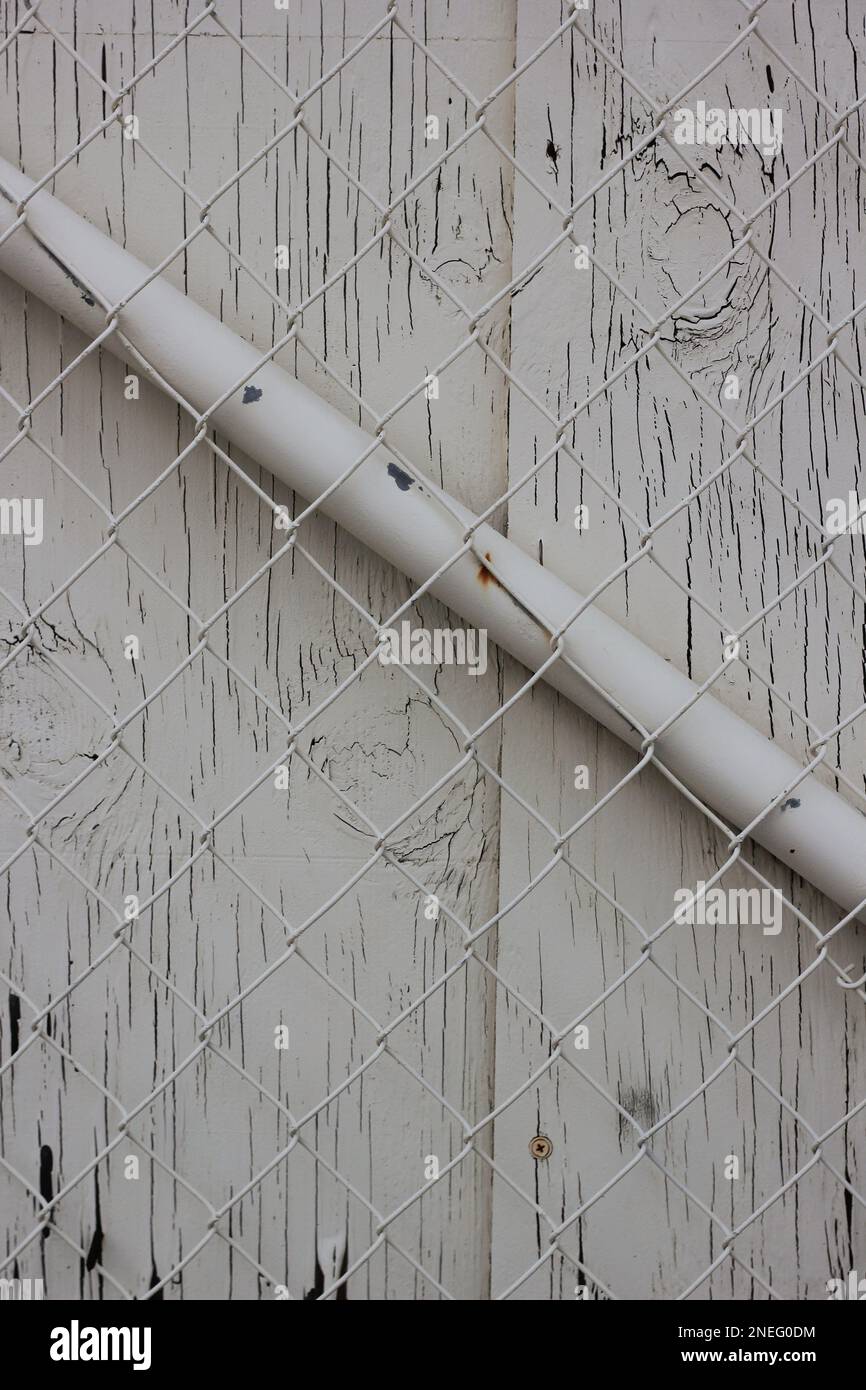 Typical common chain link fence running along a wooden wall with a pipe ...