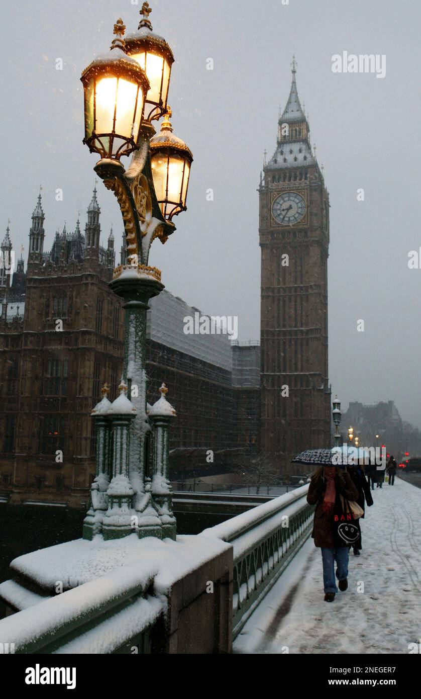 People walk across snow covered Westminster Bridge, passing the Houses ...