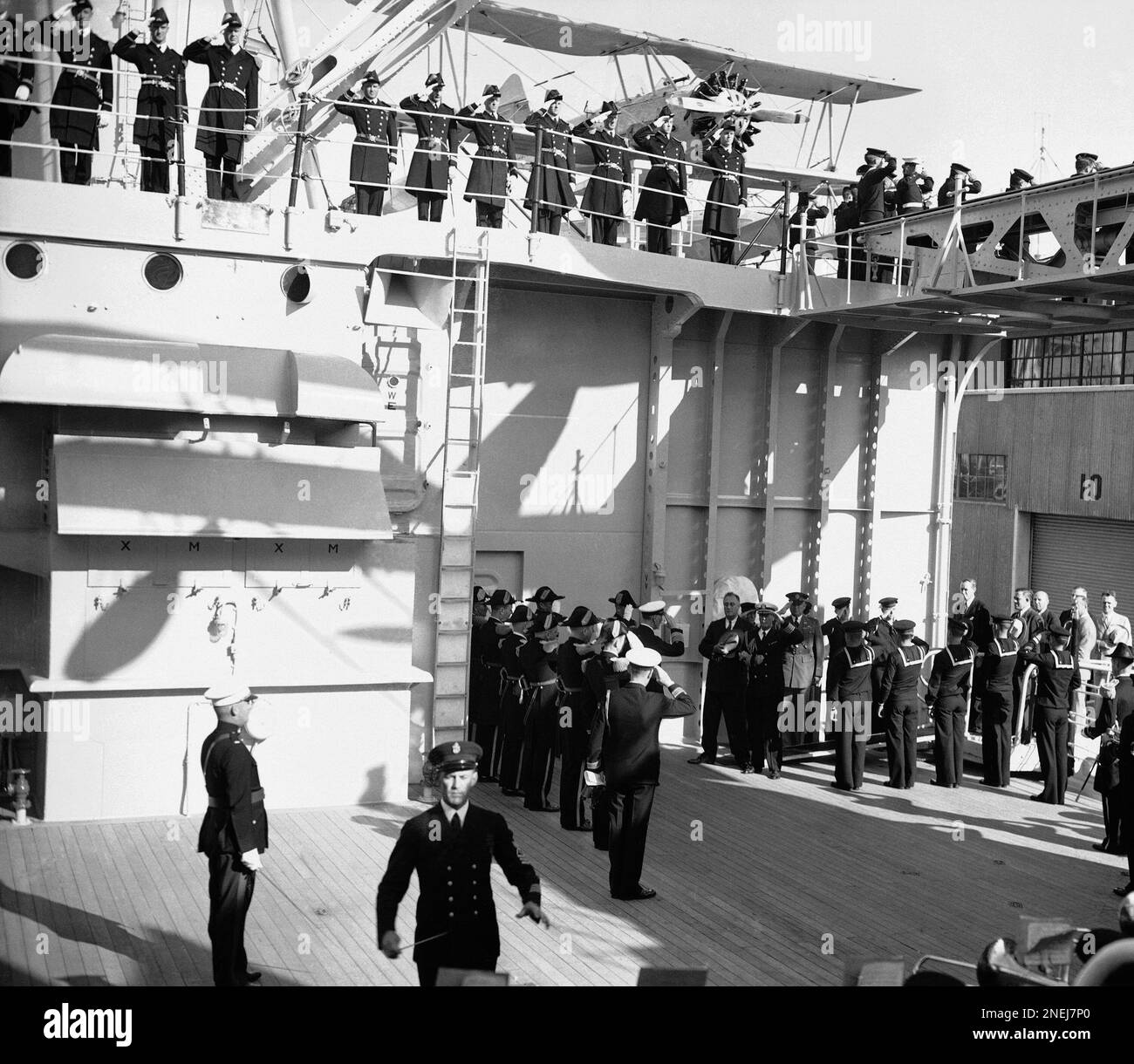 Officers and enlisted men of the U.S.S. Houston are shown saluting as ...