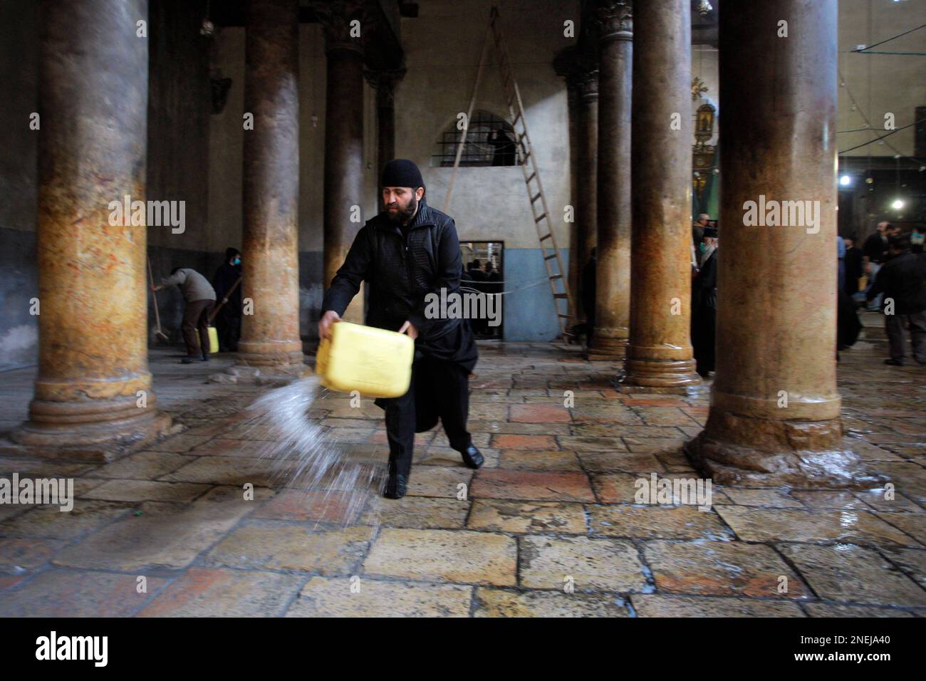 A Greek Orthodox clergyman pours water to clean the church floor during ...