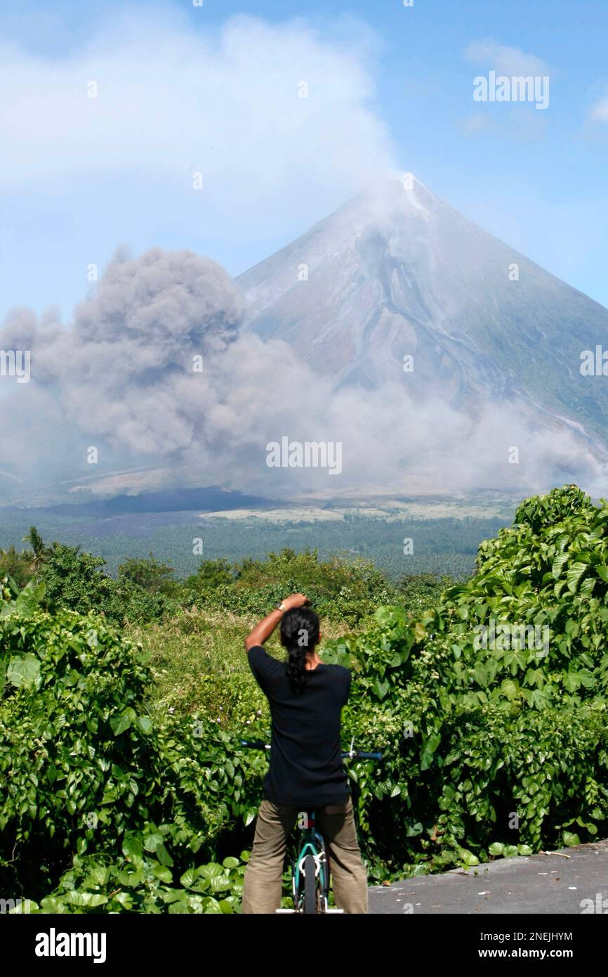 A resident pauses to take pictures of Mayon volcano emitting a column ...