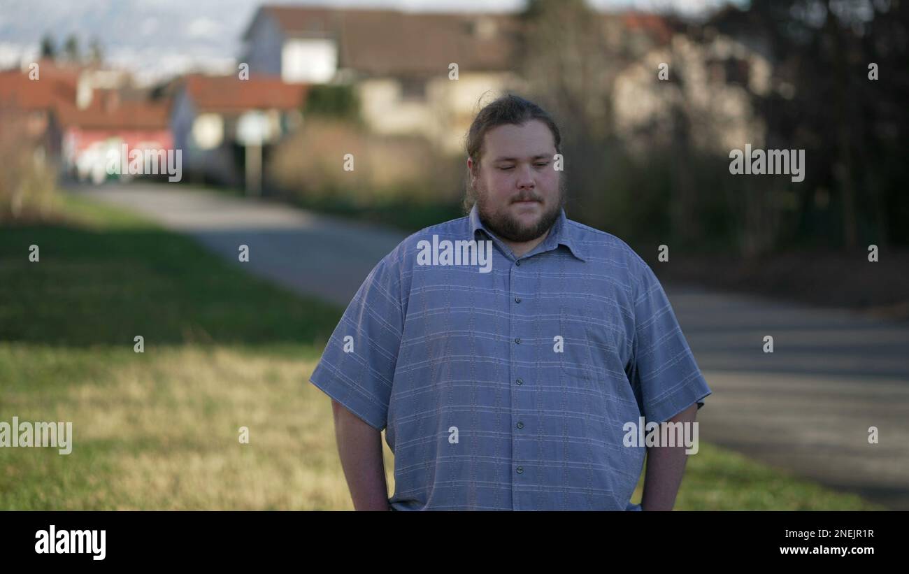 One young thoughtful chubby man standing outdoors thinking. Pensive ...
