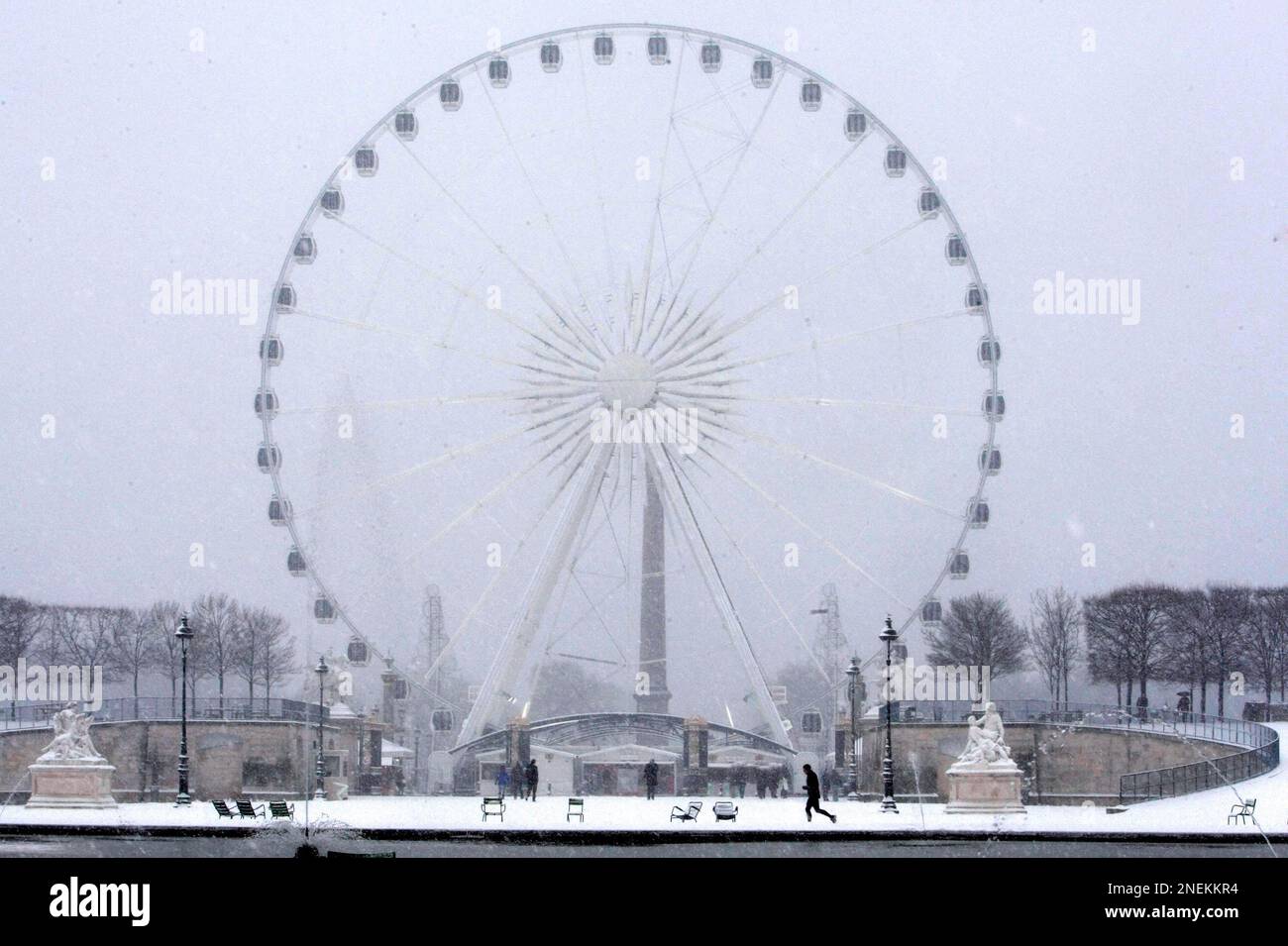 A man jogs past the ferry wheel of the Tuileries Gardens as snow falls ...