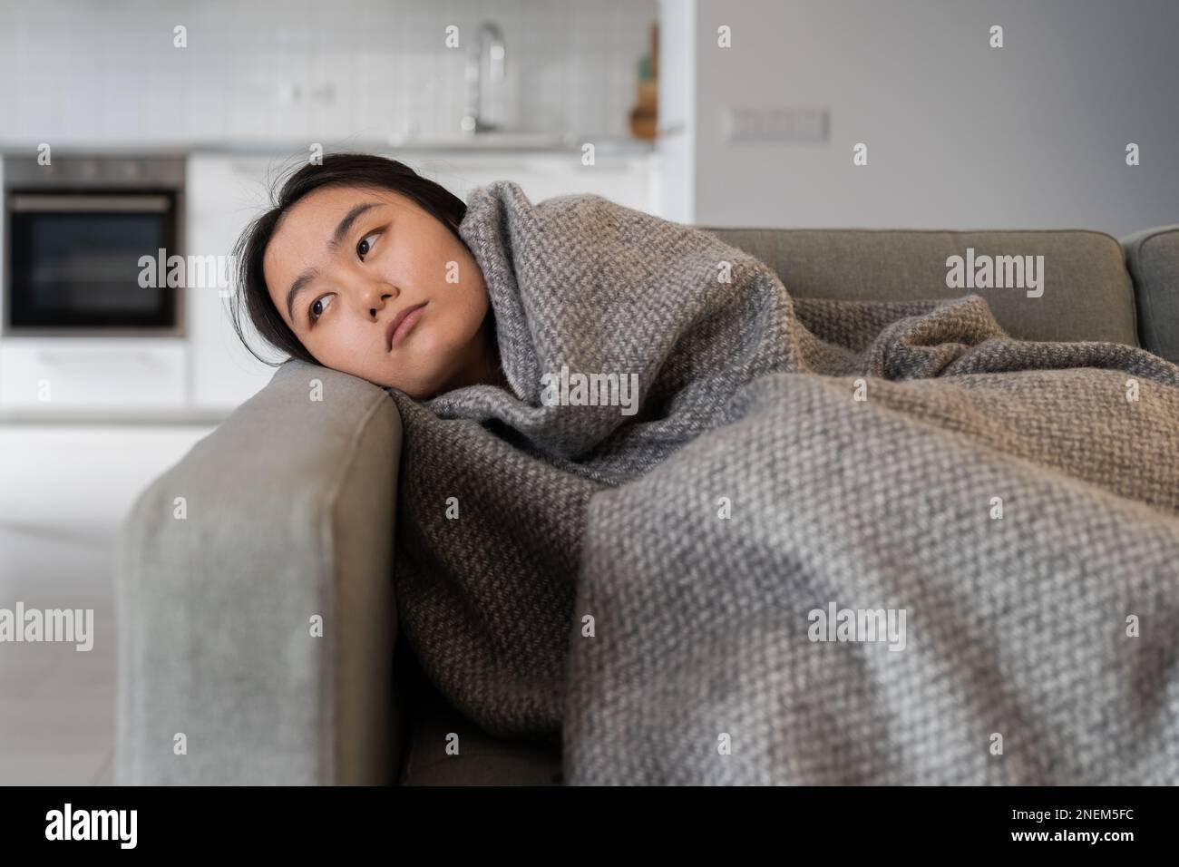 Frustrated Asian woman lying on couch looks sadly going through ...
