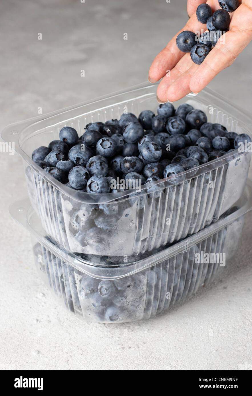 Fresh blueberries in two plastic containers on gray background, woman's ...