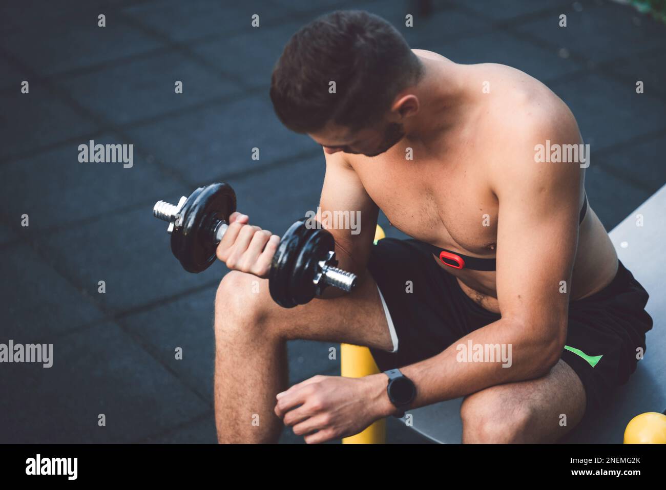Man sitting on a bench lifting weights outdoors, while wearing a sports ...