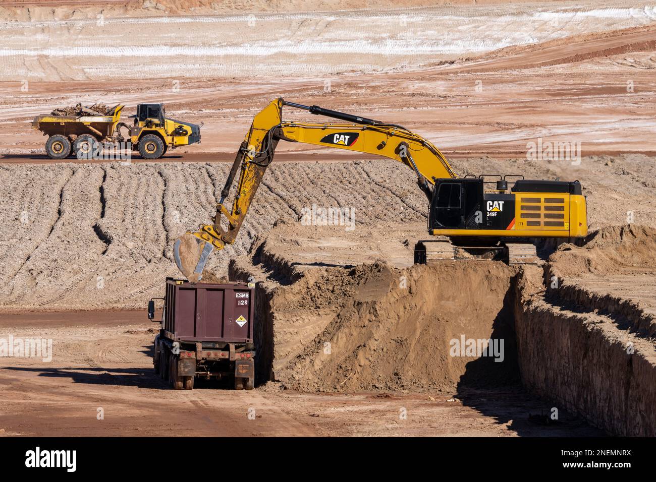 A heavy duty excavator loads a container truck with hazardous uranium ...