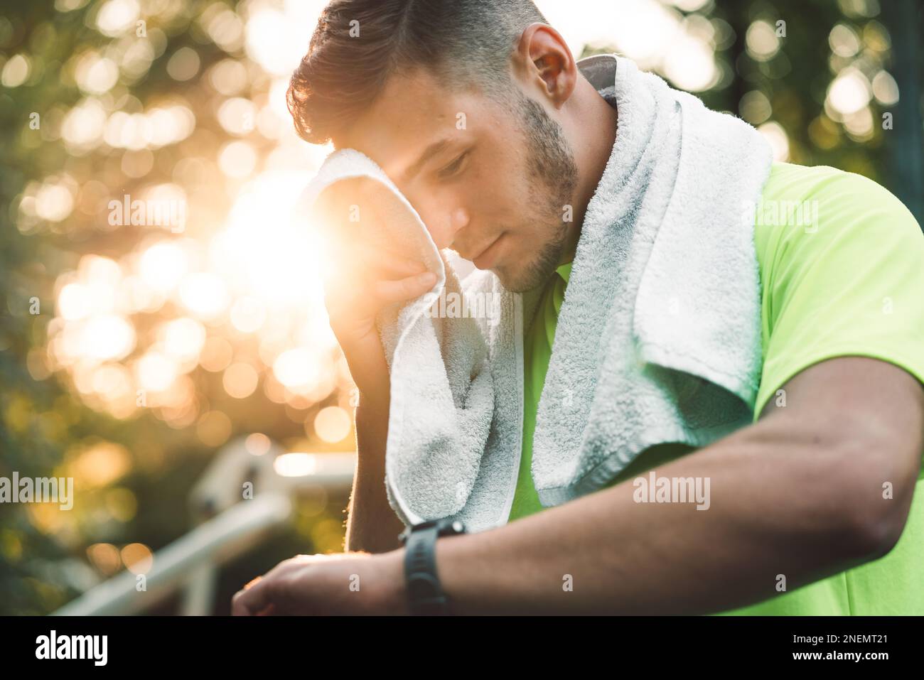 Sun flare across a young man wiping his sweat away while looking at his ...