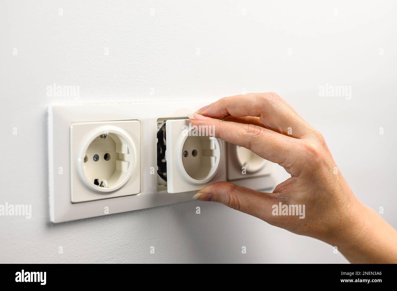 Installing a white AC wall socket with a screwdriver on a white wall ...