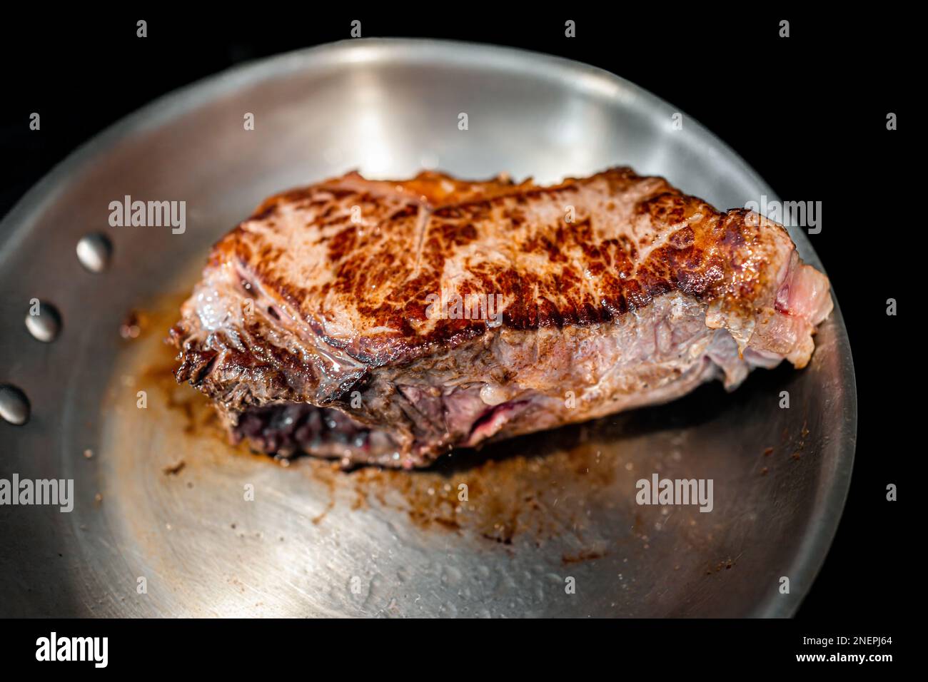 Closeup of stainless steel pan and crust on thick new york strip or ...