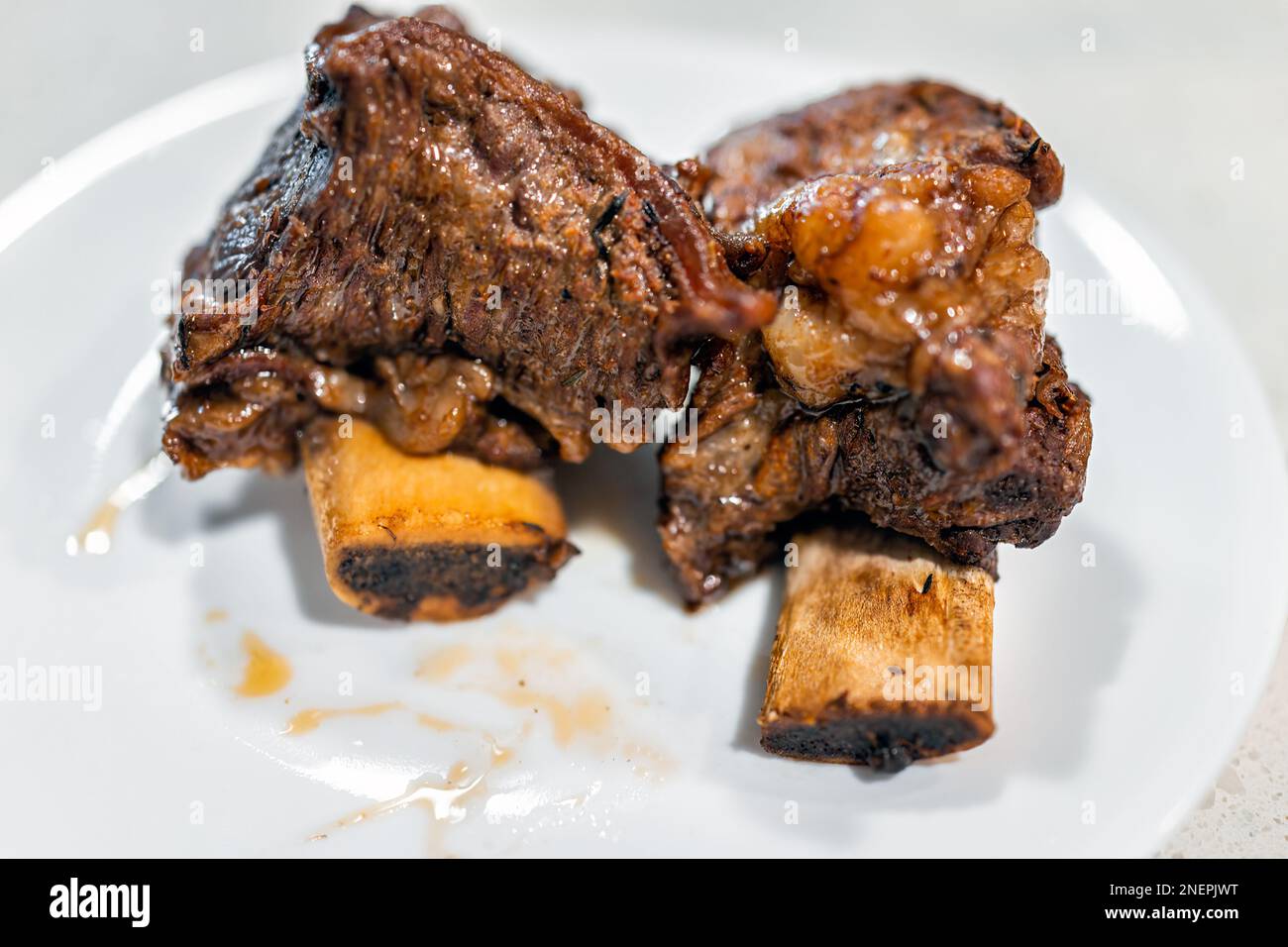Roasted bone in beef short ribs cooked brown meat on white plate macro ...