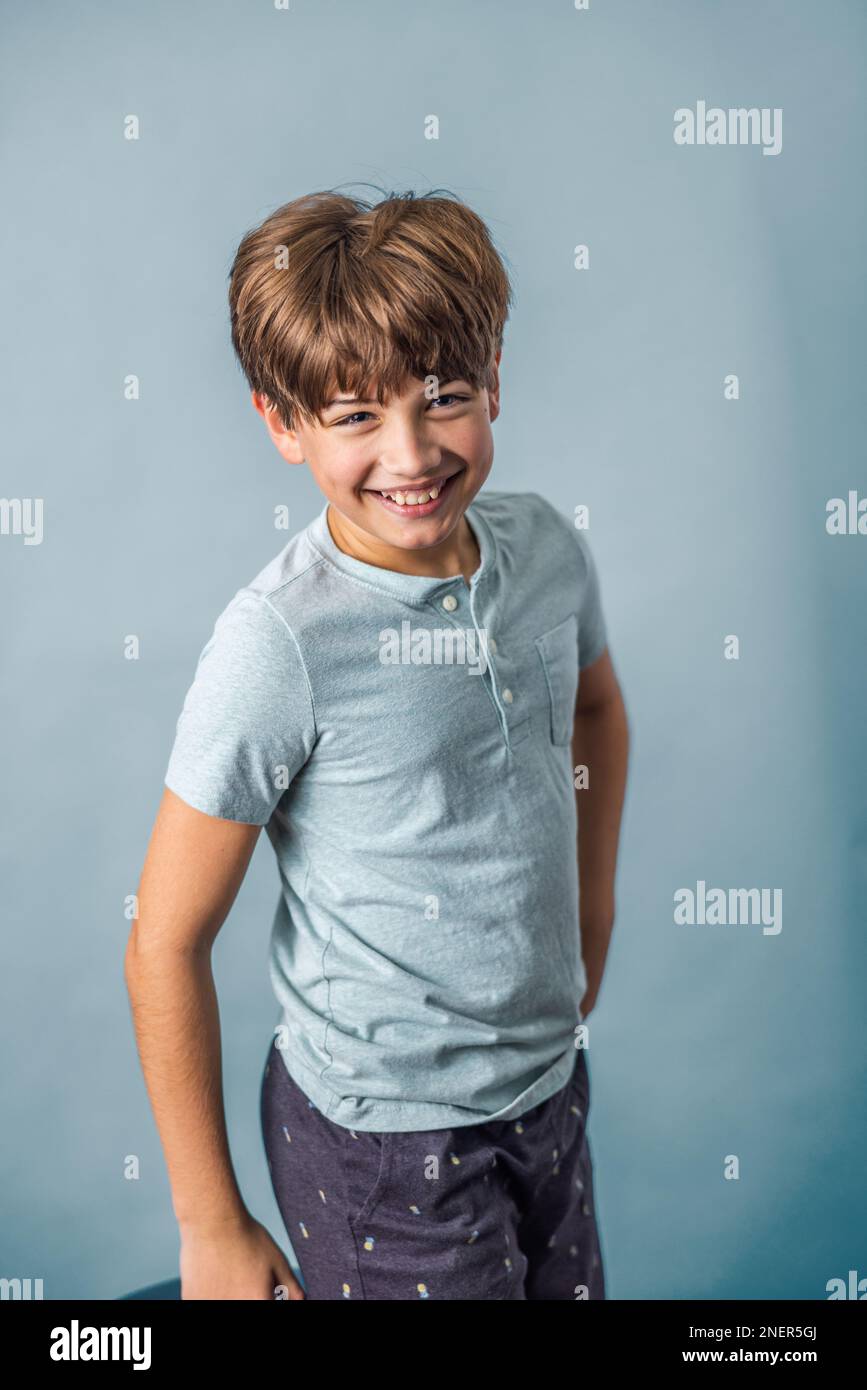 A cute pre-teen tween boy from the waist up on a muted blue backdrop ...