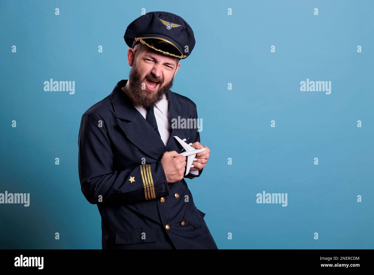 Funny pilot in uniform playing with small airplane model, aviation ...