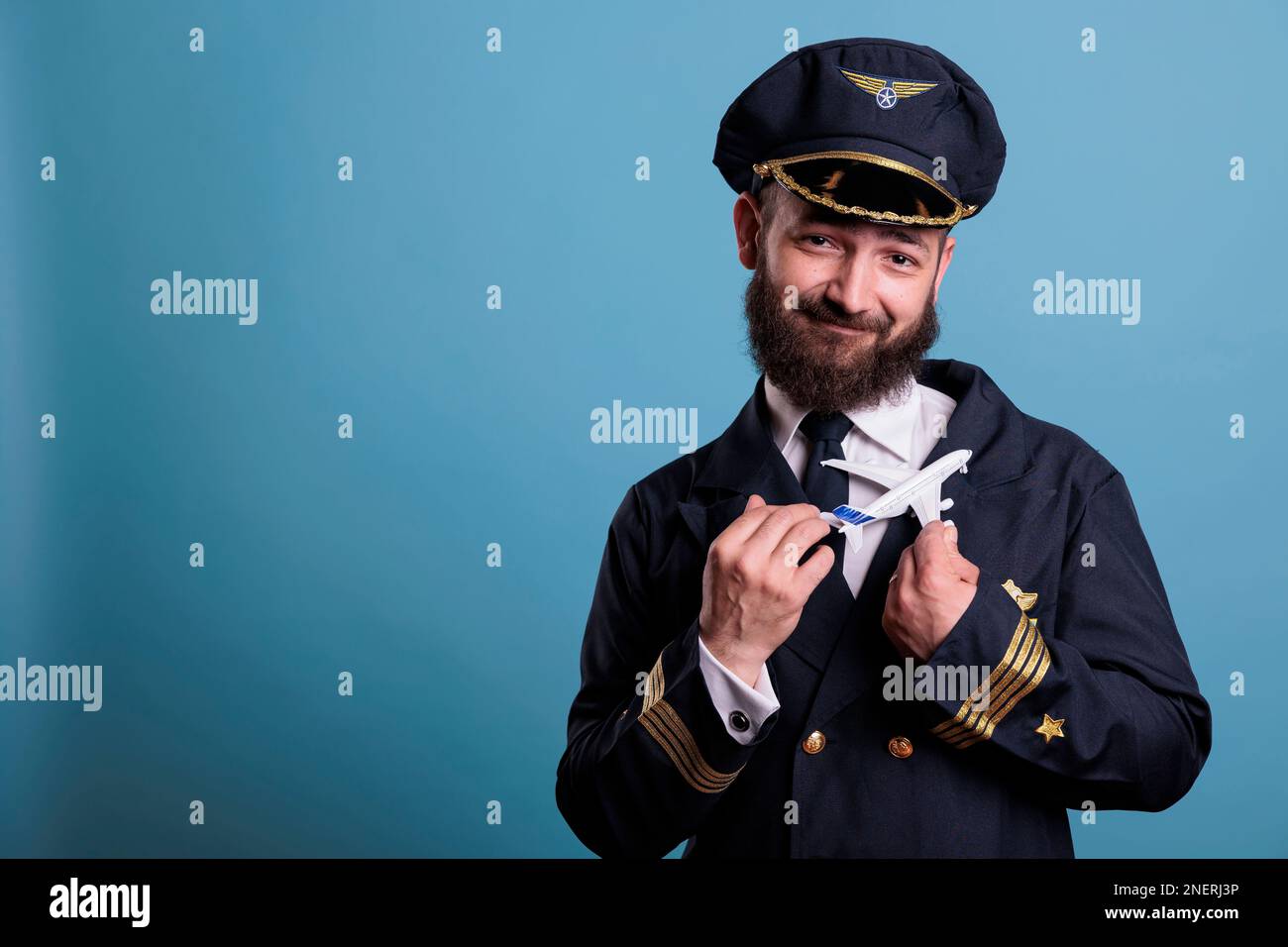 Smiling pilot in command wearing uniform holding small airplane model ...