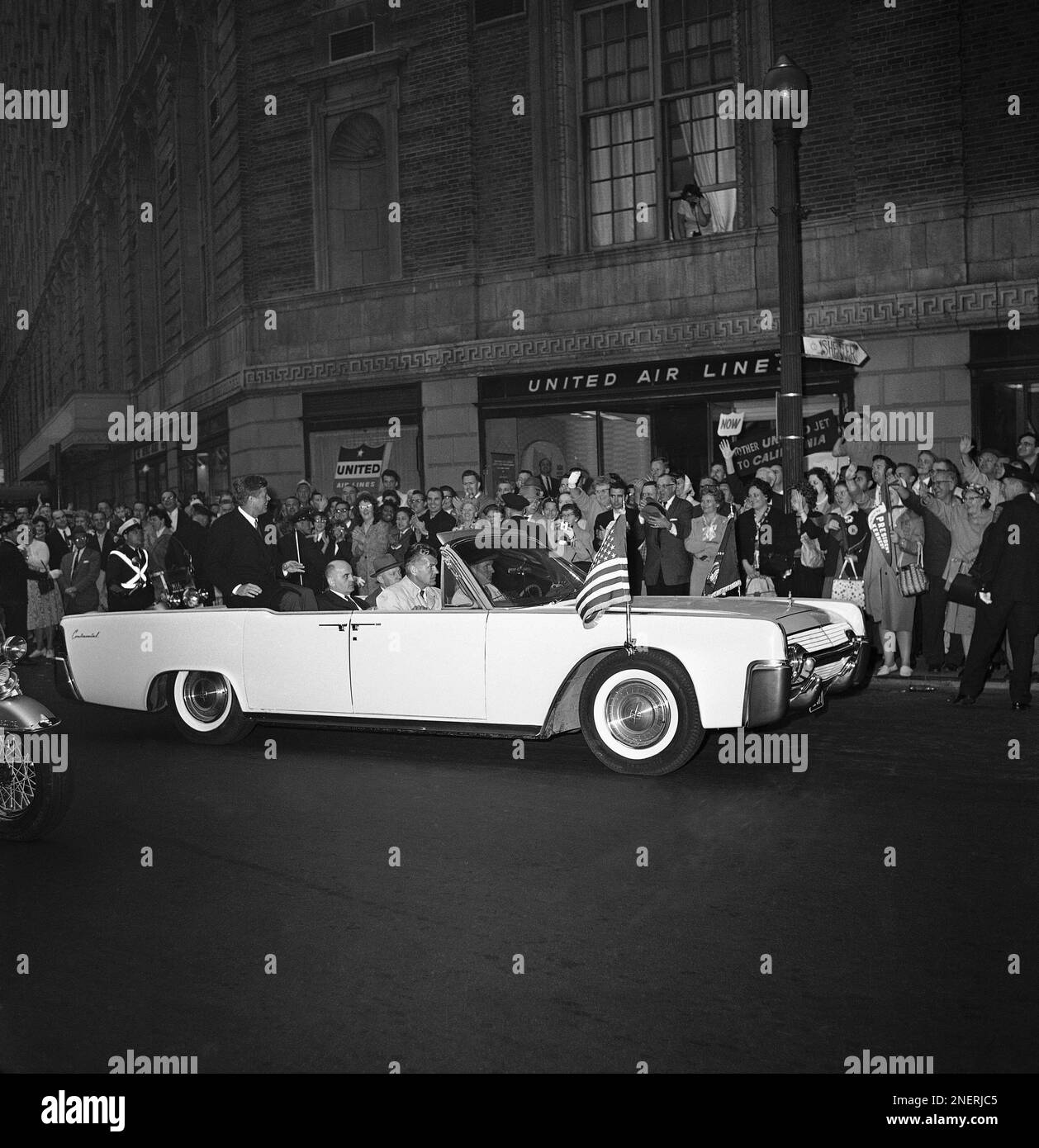 President John Kennedy sitting on rear of convertible smiles as crowd ...