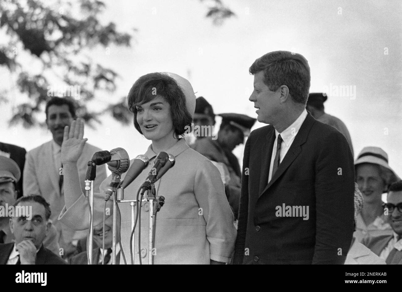 Mrs. Jacqueline Kennedy standing behind microphones with her husband ...