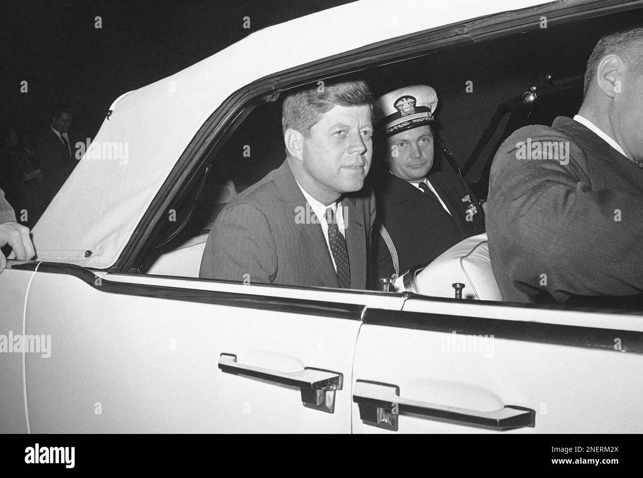 President John F. Kennedy is seated in the back of his car with his ...