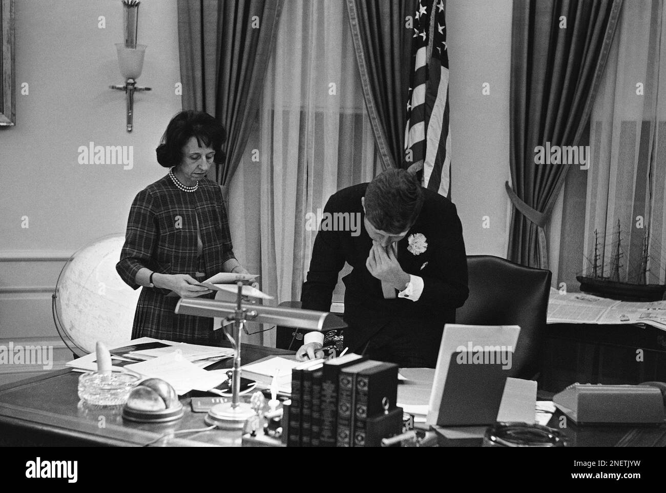 President John F. Kennedy pauses to check a piece of mail as he works ...