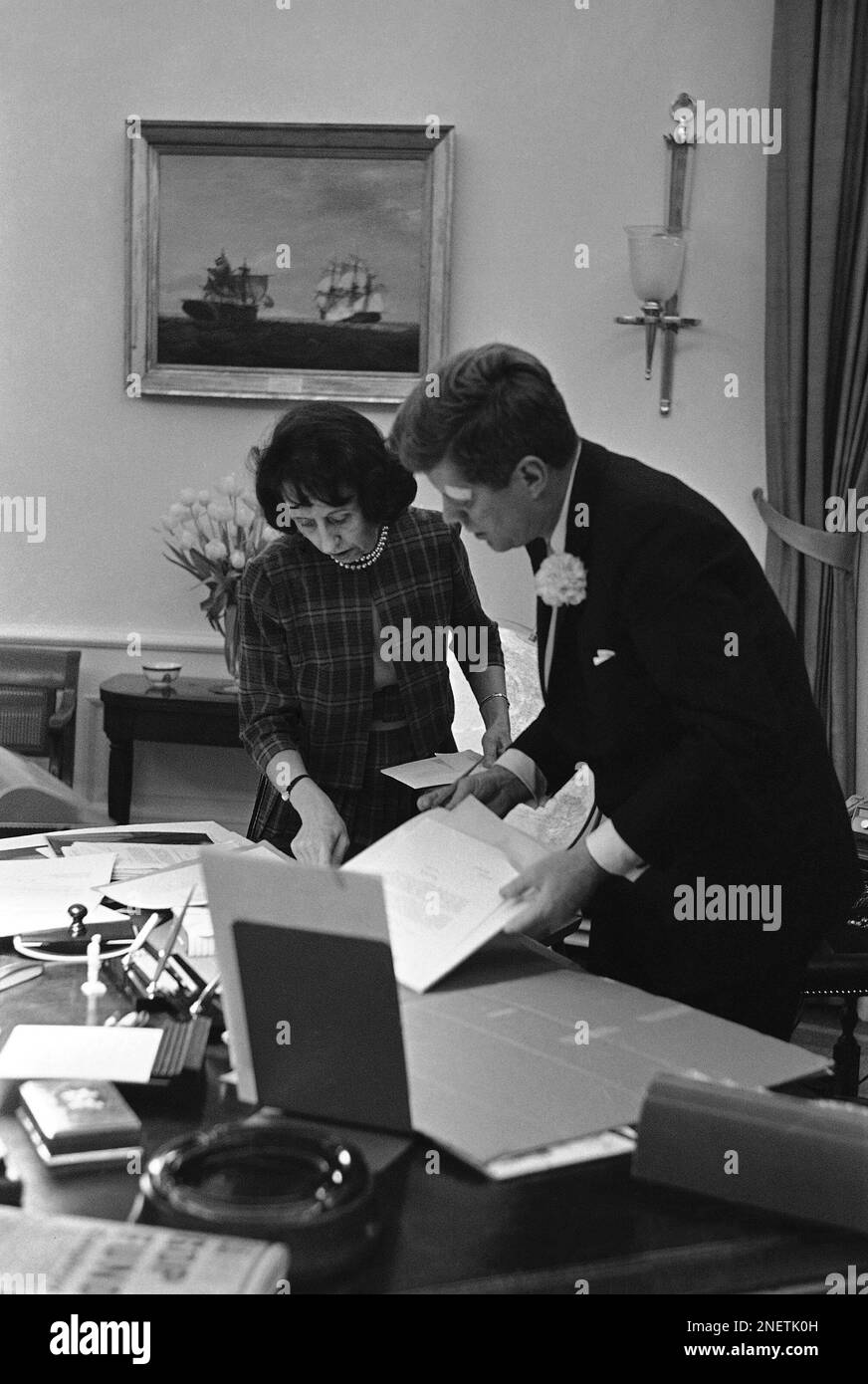 President John F. Kennedy pauses to check a piece of mail as he works ...