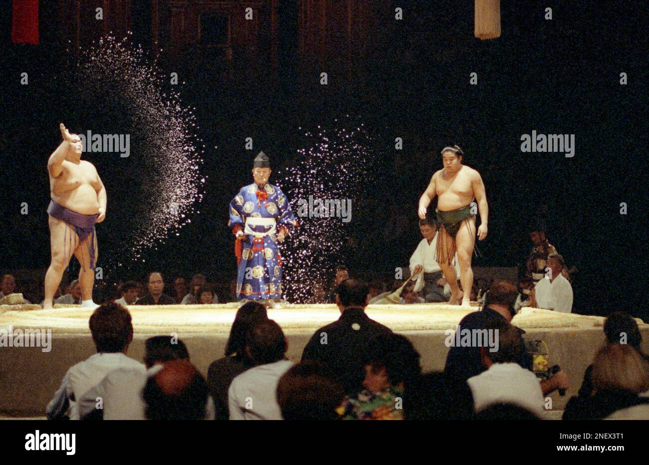 Two Sumo wrestlers throw rice into the ring watched by an umpire at the ...