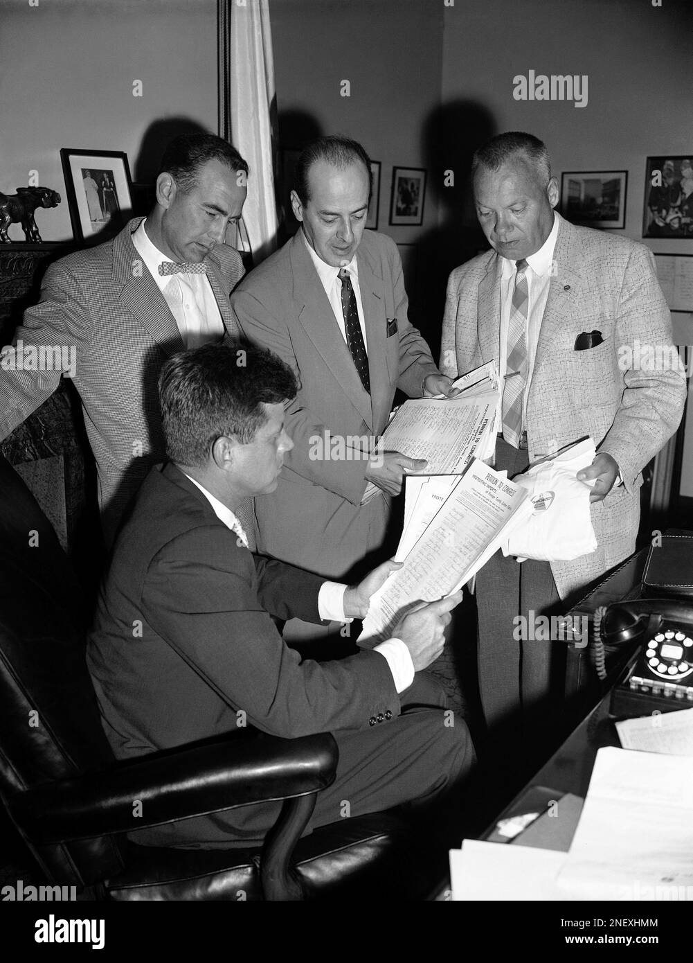 Sen. John F. Kennedy (D-Mass), seated, looks over a sheaf of petitions ...