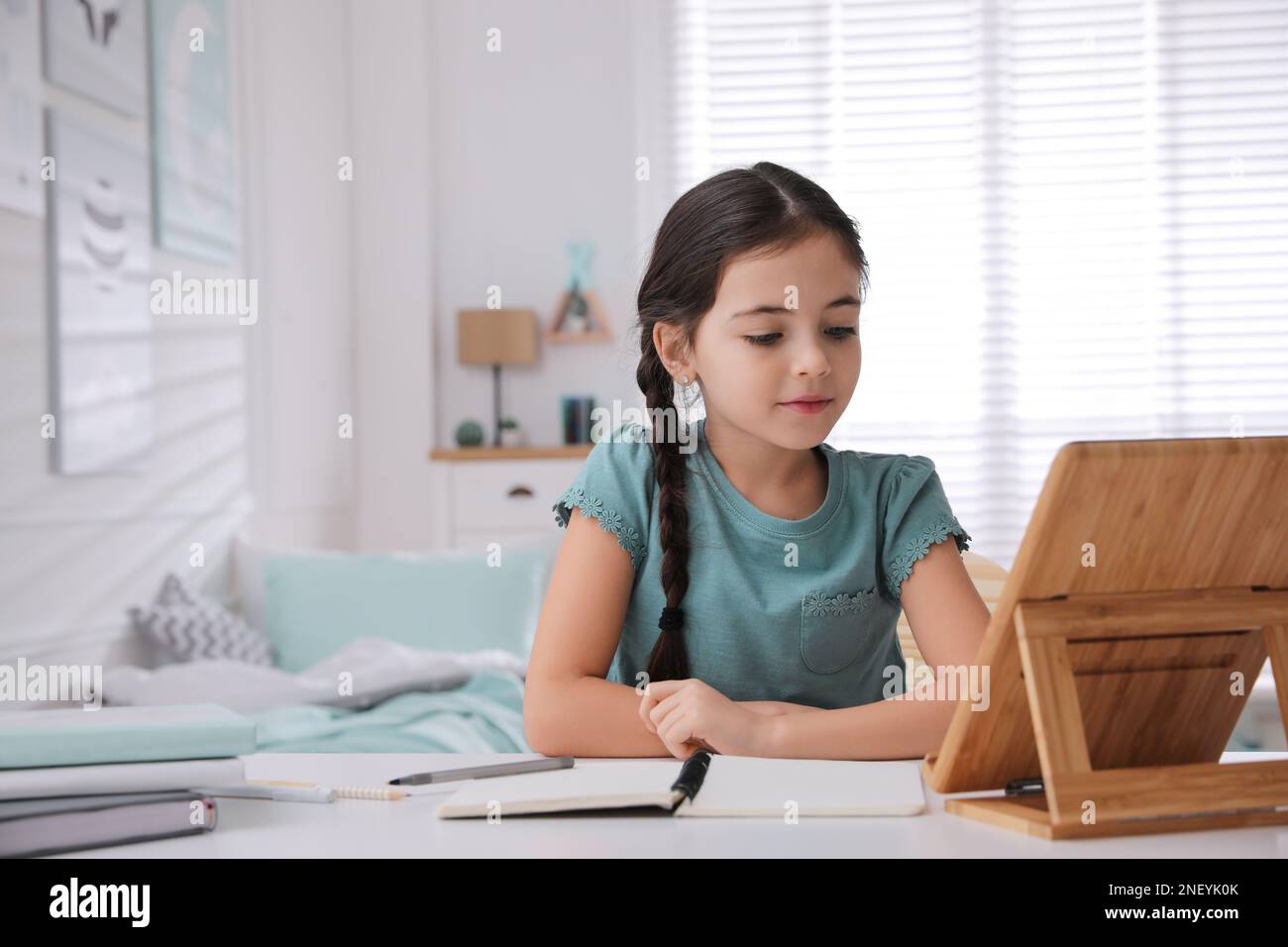Little girl doing homework with tablet at table in bedroom Stock Photo ...