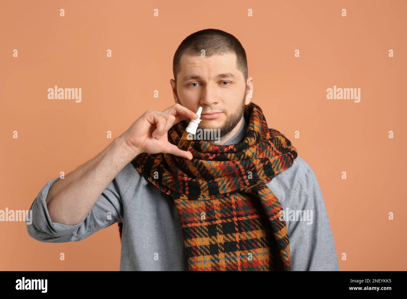 Sick man using nasal spray on orange background Stock Photo - Alamy