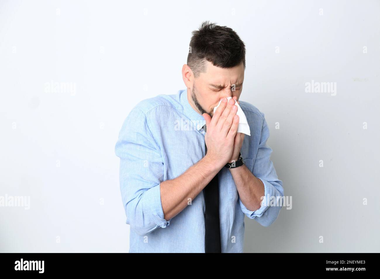 Man with tissue suffering from runny nose on white background Stock ...