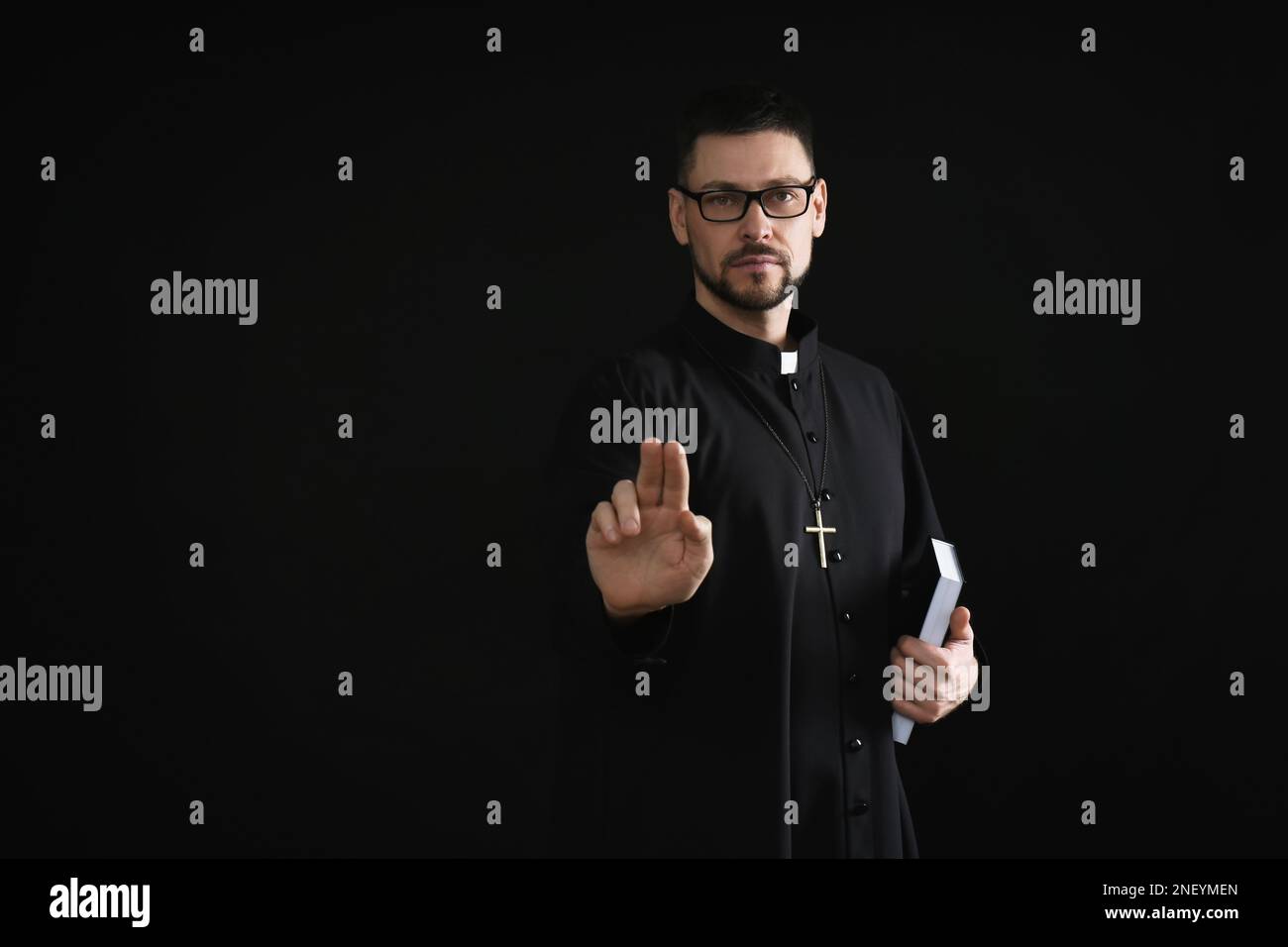 Priest with Bible making blessing gesture on dark background, space for ...
