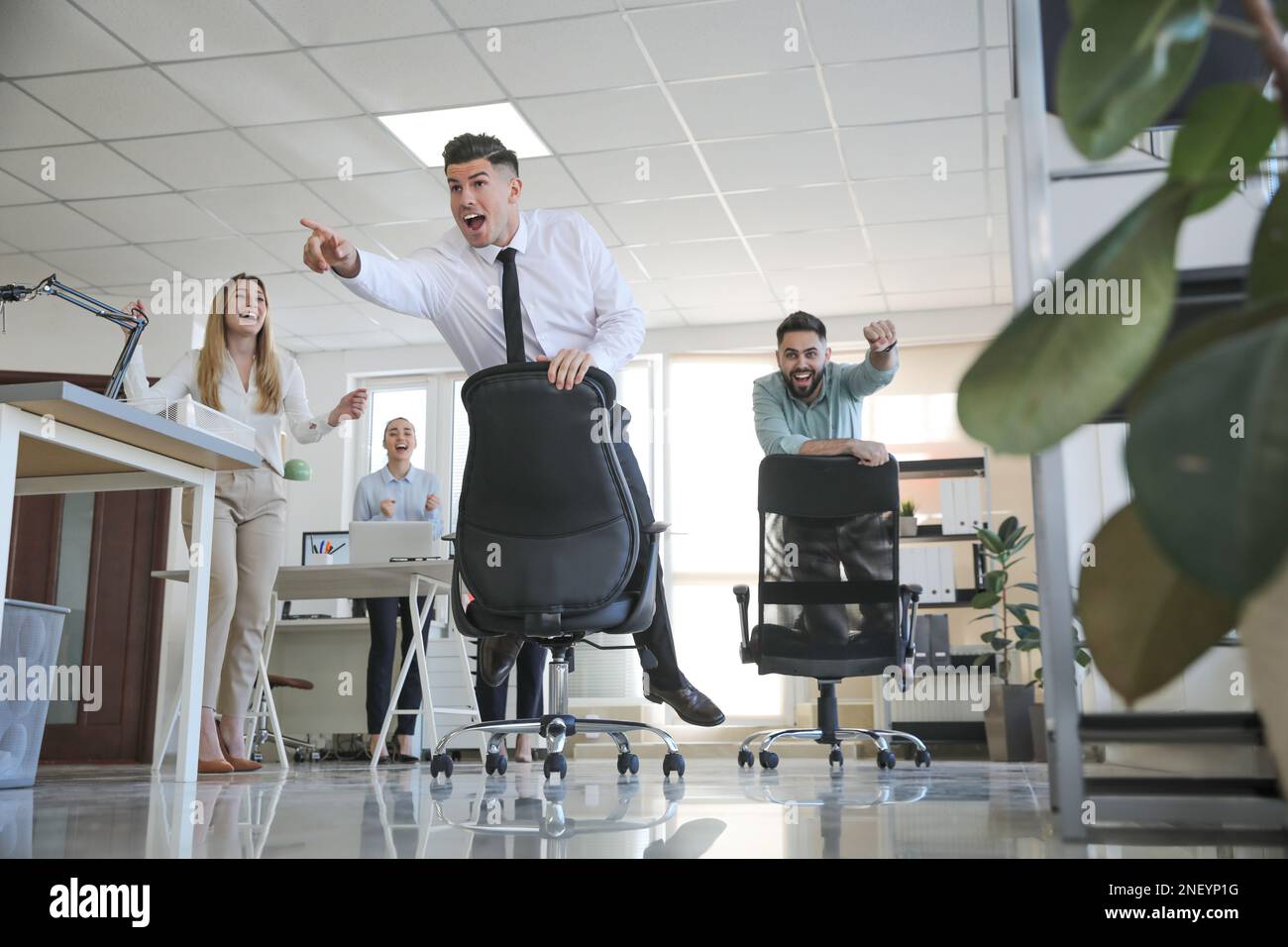 Happy office employees riding chairs at workplace Stock Photo - Alamy