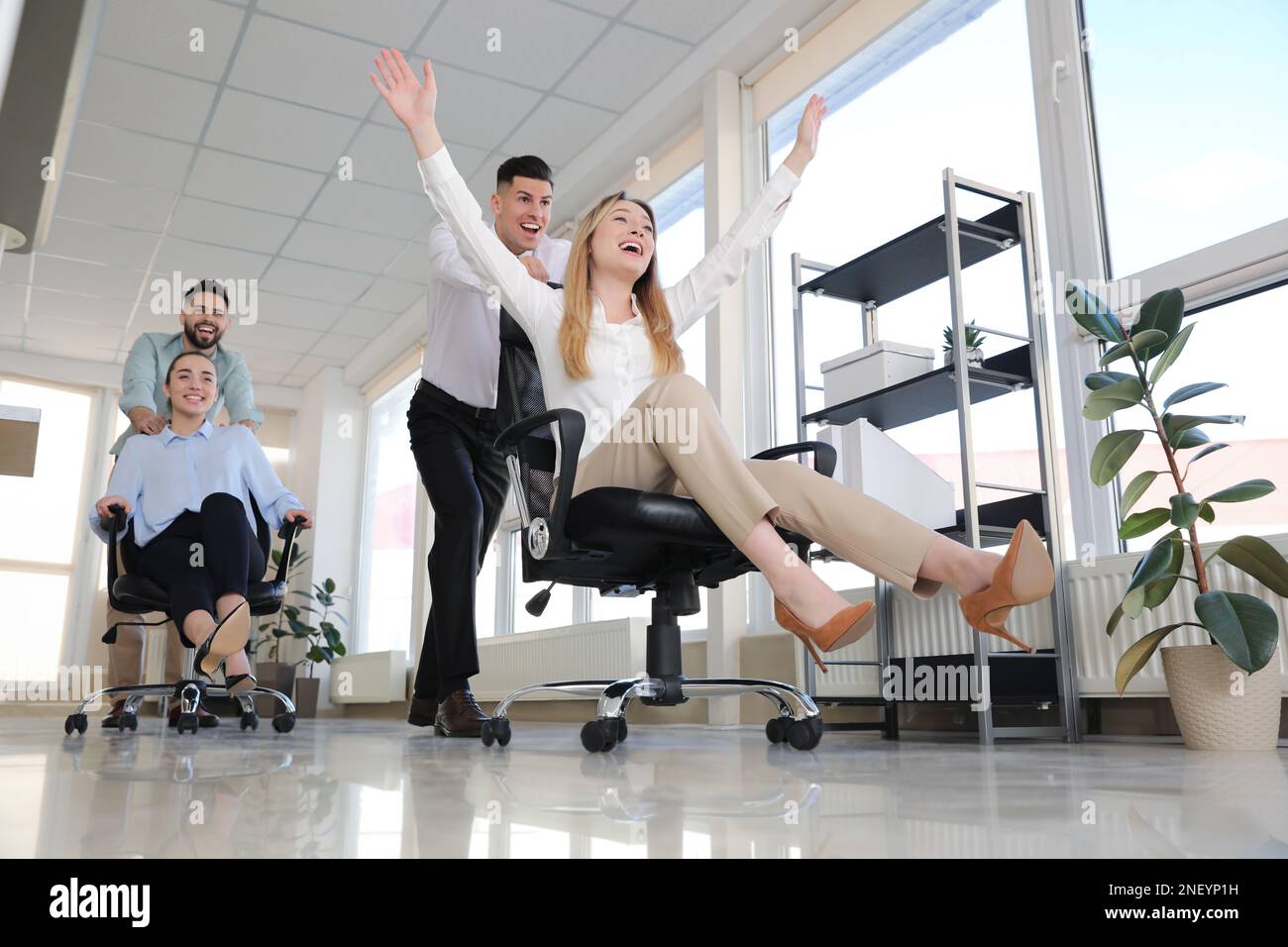 Happy office employees riding chairs at workplace Stock Photo - Alamy