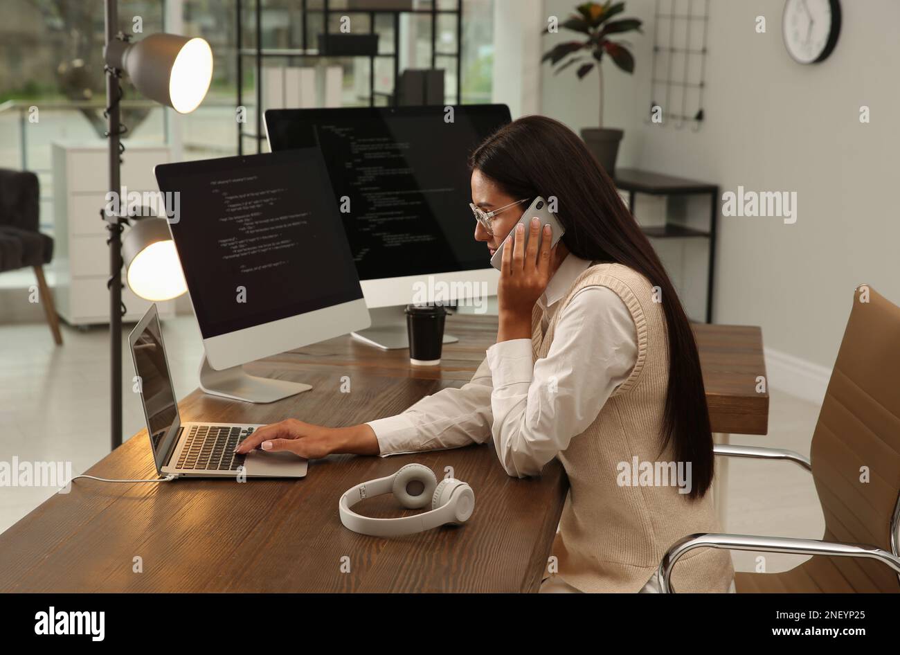 Programmer talking on phone while working at desk in office Stock Photo ...