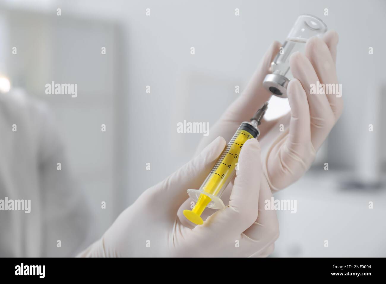 Doctor filling syringe with medication from vial on blurred background ...