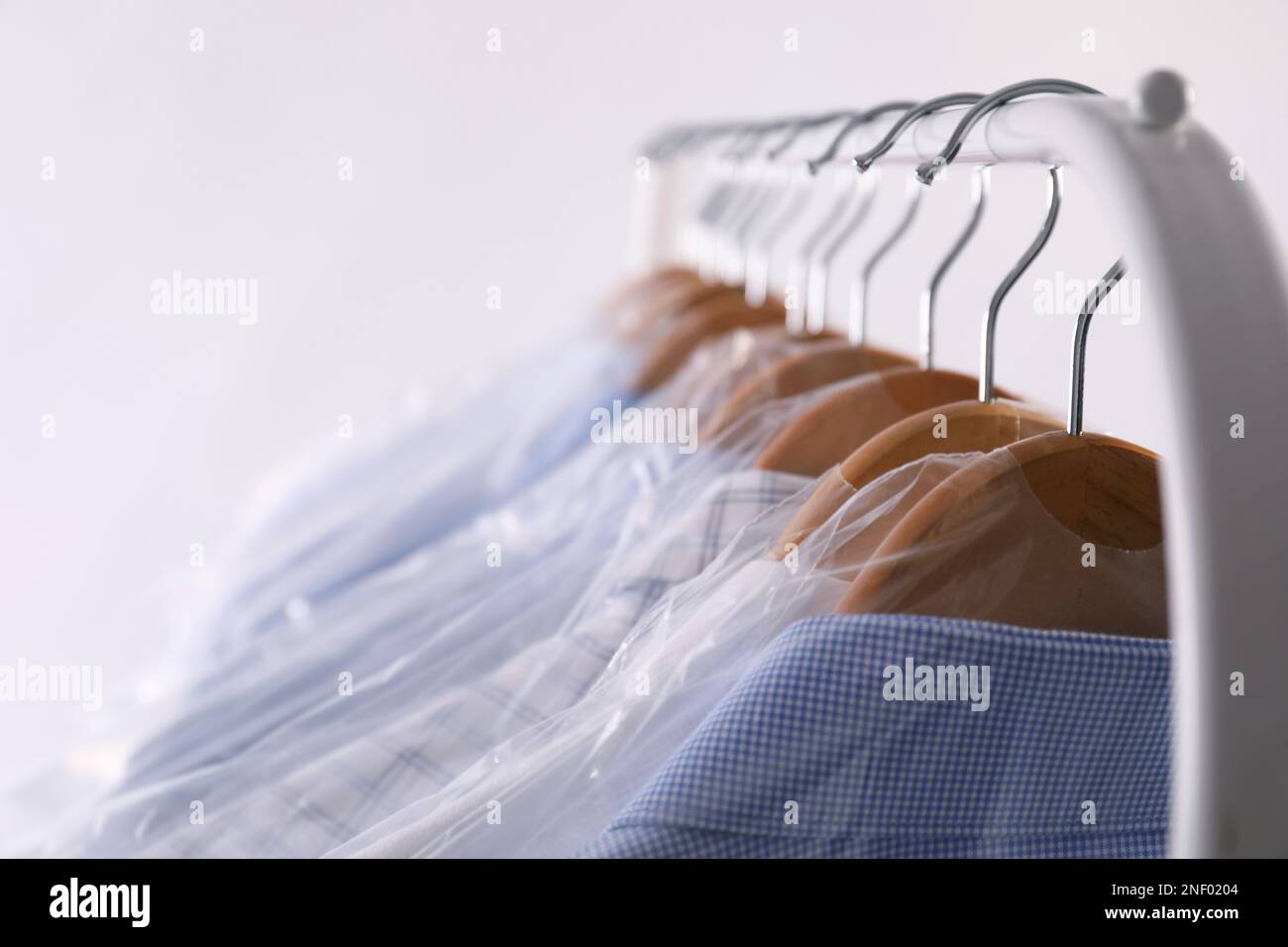 Hangers with shirts in dry cleaning plastic bags on rack against light ...