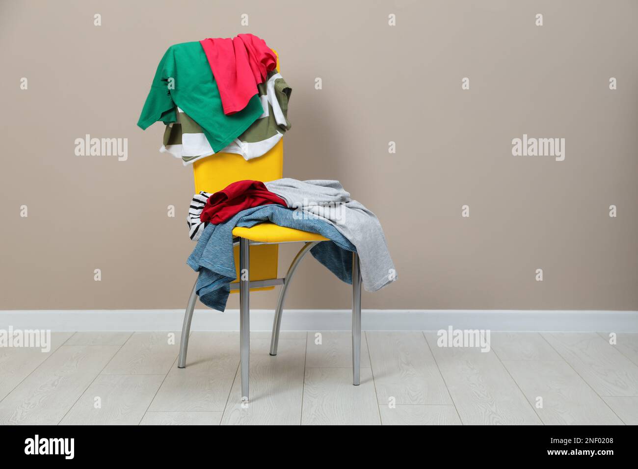 Different clothes on yellow chair near light grey wall, space for text ...