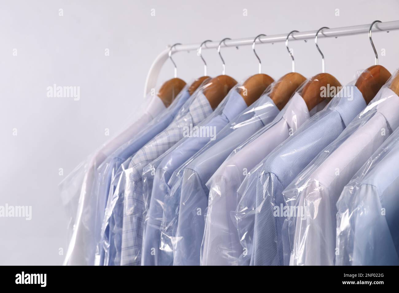 Hangers with shirts in dry cleaning plastic bags on rack against light ...