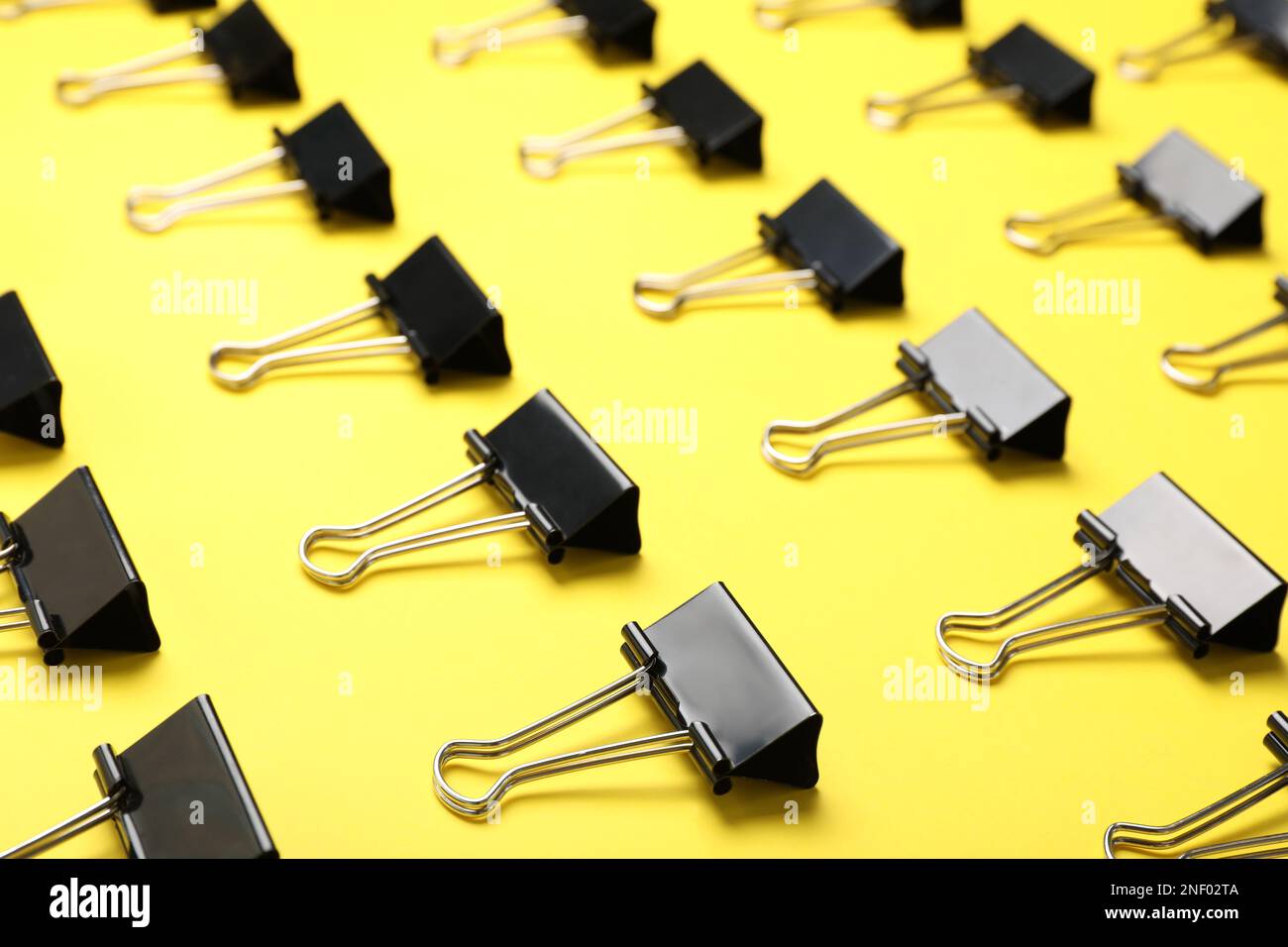 Black binder clips on yellow background. Stationery items Stock Photo ...