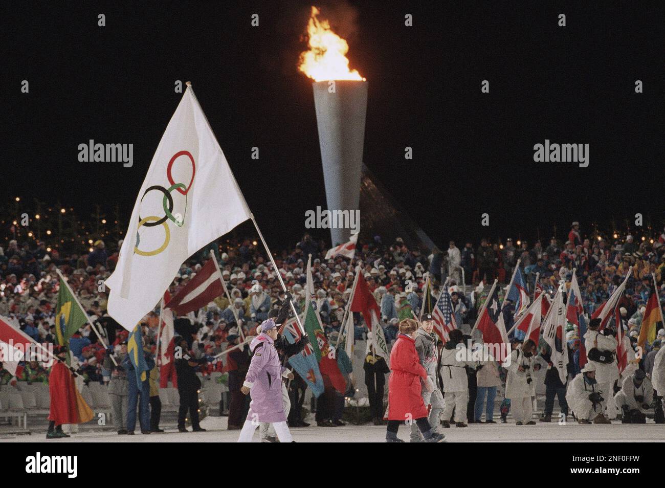 The Olympic flag is carried past athletes bearing flags and the Olympic ...