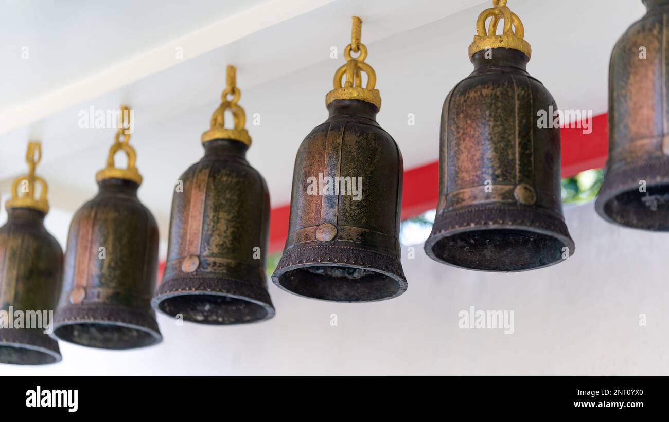 Six traditional bronze-colored bells hang one after the other against a ...