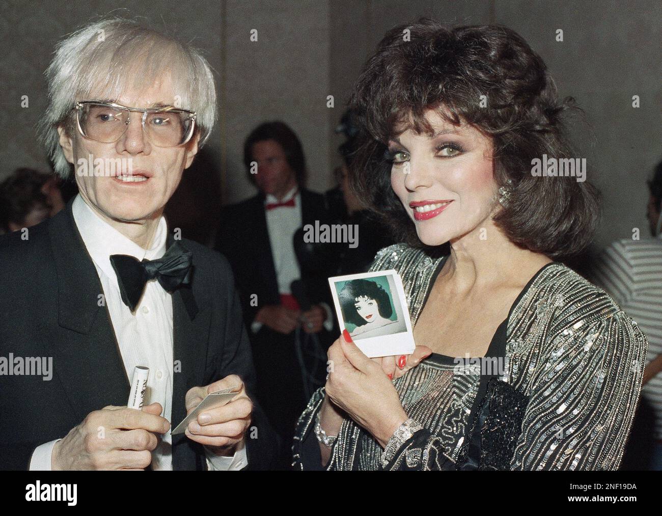 Actress Joan Collins chats with Andy Warhol, April 1, 1985. She holds a ...