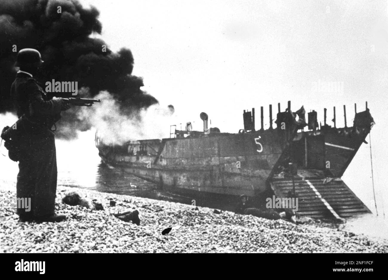 A German soldier watches a burning landing craft left on the beach at ...